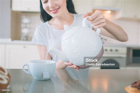 테이블에 앉아 갈색 머리의 절단 보기 그녀는 흰색 주전자를 들고 컵에 물을 붓는 다 차를 준비 하 고 있는 소녀 그녀는 부엌에서 Sitd 가정 생활에 대한 스톡 사진 및