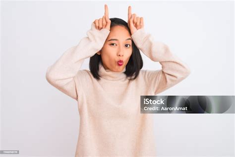 젊은 중국 여자 를 입고 터틀넥 스웨터 위에 서 고립 된 흰색 배경 을 하고 재미 제스처 와 손가락 위에 머리 로 황소 뿔 머리에 대한 스톡 사진 및 기타 이미지 Istock