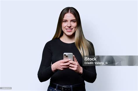 젊은 아름 다운 여자가 휴대 전화를 들고 흰색 스튜디오 배경에 카메라를 보고 20 24세에 대한 스톡 사진 및 기타 이미지 20 24세 20 29세 Brand