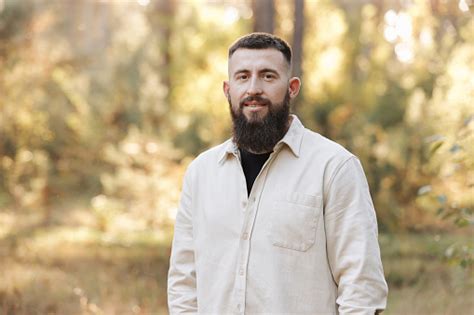 흰색 캐주얼 재킷을 입은 젊은 웃는 수염 난 남자의 초상화는 시골이나 공원의 가을 자연 배경에서 카메라를 봅니다 스타일의 개념