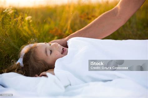 소녀는 풀밭의 하얀 침대에서 자고 신선한 공기를 마신다 아빠의 손이 부드럽게 머리를 두드린다 보살핌 보호 국제 어린이날 모기에 물린 2명에 대한 스톡 사진 및 기타 이미지