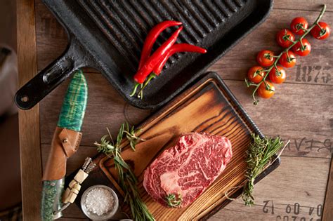 로즈마리 잔가지 가지에 붉은 토마토 소금과 후추 붉은 칠리 페퍼 포드 나무 표면에 그릴 팬이 있는 도마에 신선하고 육즙이 많은 리브아이 스테이크 프리미엄 스테이크 를 요리