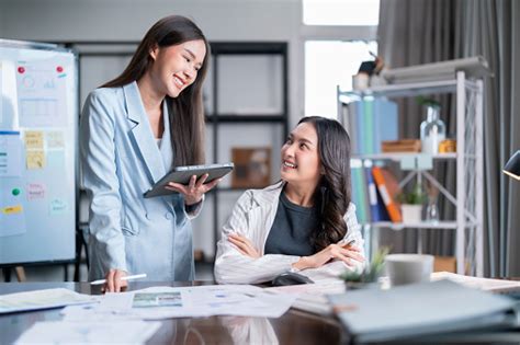 아시아 파트너 비즈니스 여성은 노트북 태블릿 종이 차트 문서를 사용하여 가능한 다가오는 프로젝트에 대해 이야기합니다젊은 여성은 프로젝트에 최종 아이디어를 준비하고 추가합니다