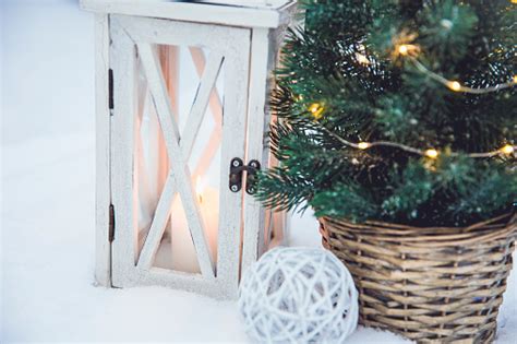 흰색 왁스 촛불이 있는 흰색 나무 랜턴과 작은 크리스마스 전나무 나무 눈 속의 갈색 등나무 화분에 마이크로 Led 조명 눈 덮인 전나무 나무 겨울에 야외 공간을 복사합니다