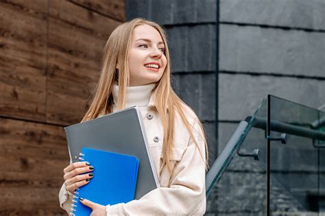학생 소녀는 손에 폴더 노트북 책을 들고 미소를 지으며 현대 대학 건물의 배경을 바라 봅니다 노트북에 대한 스톡 사진 및 기타 이미지 Istock