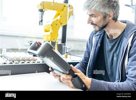 skilled worker in robotic factory controlling robot arm with digital