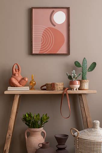 모형 포스터 프레임 나무 콘솔라 화분에 담긴 식물 꼰 바구니 조각품 베이지색 벽 및 개인 액세서리가 있는 따뜻한 거실 인테리어의