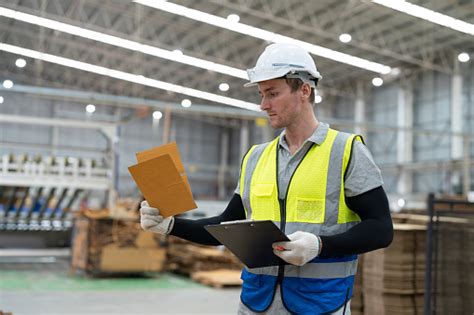 종이 공장에서 고품질 제품을 확인하는 판지 시트를 들고 있는 남성 엔지니어 조끼와 헬멧 안전을 착용하고 골판지 상자 생산