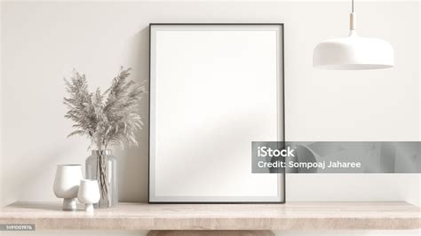 빈 검은색 포스터 프레임 모형입니다 나무 캐비닛 가구에 유리 화병 조각품 및 램프에 말린 꽃을 놓습니다 하얀 방 배경 크림색