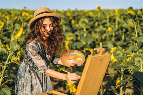 곱슬머리와 모자를 쓰고 있는 한 젊은 여성이 자연속에서 그림을 그리고 있습니다 아름다운 날에 해바라기 밭에 서있는 한 여성 개념에 대한 스톡 사진 및 기타 이미지 Istock