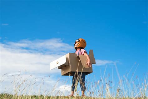 화창한 날에 초원에서 골판지 비행기를 가지고 노는 귀여운 몽상가 어린 소녀 푸른 여름 하늘 배경에 골판지 비행기로 노는 행복한 아이 어린 시절의 꿈 상상력 개념 아이에 대한