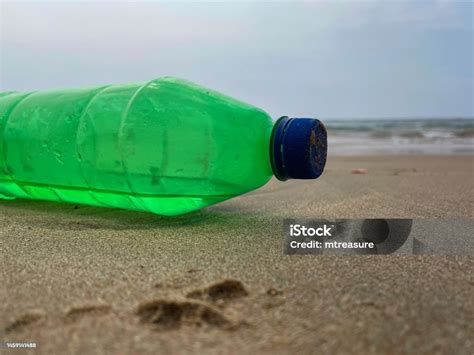 썰물 가장자리의 모래 사장에 씻겨 내려간 파란색 뚜껑이 있는 빈 녹색 플라스틱 음료수 병의 클로즈업 이미지 해안의 바다 쓰레기와 오염을 씻는 파도 흩어지는 모래 더러운 해변