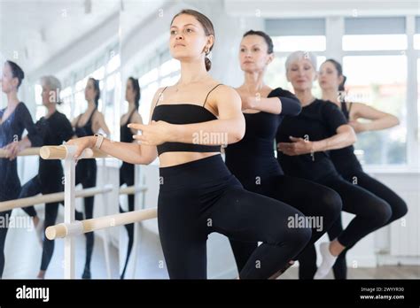 Young Girl Practicing In Passe Position At Barre During Group Ballet