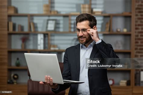 성숙한 사업가 변호사는 사무실에서 일하며 웨이터는 노트북 안경을 쓴 고위 상사 사무실 내부의 비즈니스 정장 웃는 남자를 사용합니다 변호사에 대한 스톡 사진 및 기타 이미지