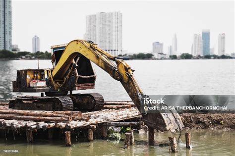 굴삭기 또는 굴착기계 작업용 양동이는 나무 기초 기둥에 의한 강둑 붕괴를 보호하기 위한 제방의 건설 현장의 과정을 운하에 파고 있다 0명에 대한 스톡 사진 및 기타 이미지