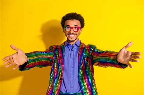 밝은 노란색 배경을 배경으로 두 팔을 벌리고 쾌활하게 포즈를 취하는 활기찬 여러 가지 빛깔의 재킷을 입은 카리스마 넘치는 젊은이