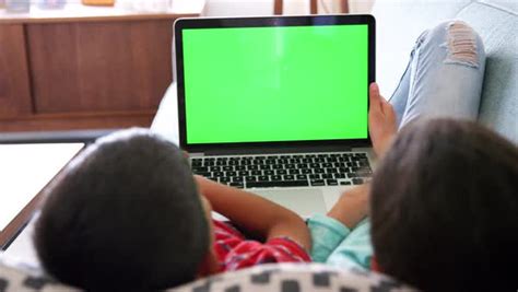 Rear View Of Brother And Sister Lying On Sofa At Home Using Laptop