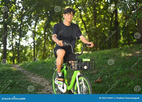 Handsome Asian Man Riding Bike Through A Serene Park On Sunny Day