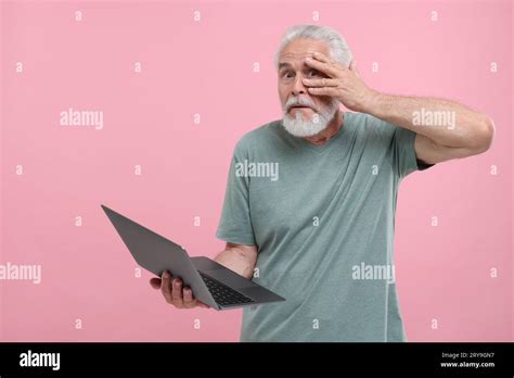 Embarrassed Senior Man Holding Laptop On Pink Background Space For