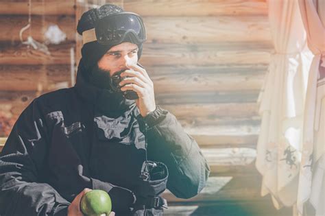 수염 행복 Snowboarded 타고 세션 후 나머지를 복용 햇볕이 잘 드는 테라스에서 따뜻한 차 한잔 마시는 젊은 남자 흐리게 배경입니다 수평 거울에 대한 스톡 사진 및