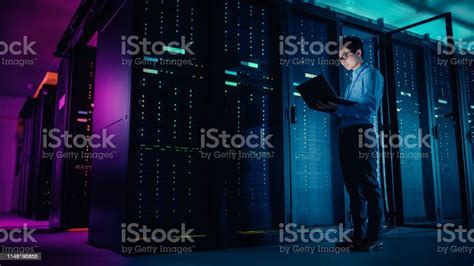 데이터 센터 랩톱에서 유지 관리 프로그램을 실행 하는 남성 It 기술자는 운영 서버 랙을 최적의 기능으로 제어 합니다 네온 색깔 빛에 있는 현대 하이테크 운영 최고 컴퓨터