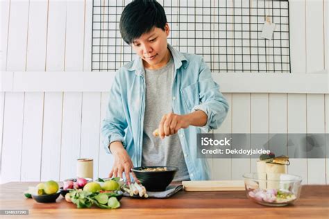 미소 짓는 아시아 남자는 통조림 생선 샐러드 메뉴 태국 음식을 만들기 위해 야채와 테이블에 그릇에 넣어 신선한 레몬 주스를 짜냅니다 집에서 부엌에서 준비를 요리하는 사람들