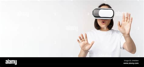 Amused Asian Girl Using Vr Glasses Virtual Reality Headset And Reaching Hands Into Empty Space