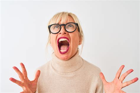 고립된 흰색 배경 위에 터틀넥 스웨터와 안경을 착용한 중년 여성은 공격적인 표정과 팔을 들고 미친 듯이 외치고 소리쳤다 좌절 개념입니다 감정에 대한 스톡 사진 및 기타