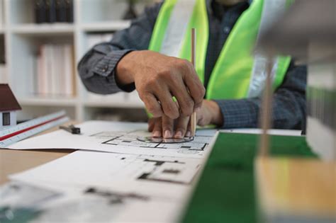 사무실에서 일하는 집의 모델을 가진 사업가 또는 건축가 청사진을 가지고 사무실에서 일하는 건축가 엔지니어는 건축 계획을 검사하고 건설 프로젝트를 스케치하고 사업 개념을