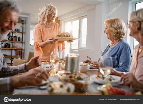 Happy Senior Woman Serving Bread While Talking Her Friends Dining