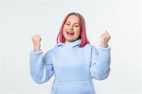 열정적 인 쾌활한 젊은 여성은 축하하고 승리하고 목표를 달성하고 기쁘게 웃는다 흰색 배경 위에 서 있는 파란색 까마귀에 분홍색 머리를 가진 사랑스러운 여성 모델 30 34