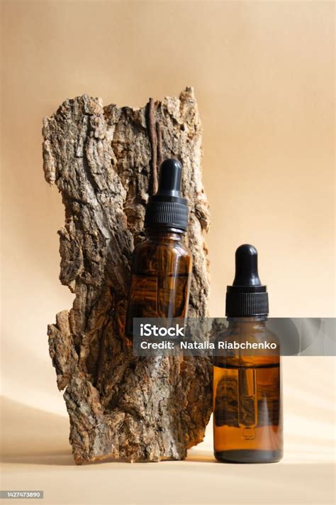 나무 껍질로 만든 스탠드에 점적기 뚜껑이있는 호박색 유리 병 두 개의 모형 햇빛 아래 베이지 색 배경에 콜라겐 보습 히알루 론산