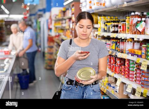 Woman Customer Scanning Barcode On Aluminum Canned Food With Smartphone While Shopping In