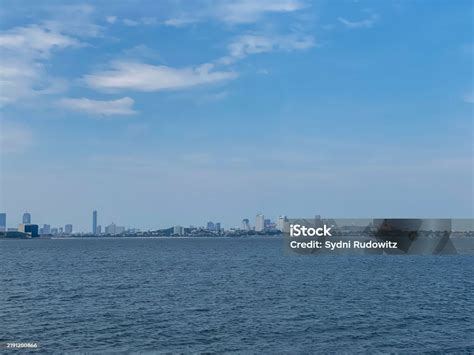 부드러운 흰 구름이 있는 밝은 푸른 하늘 아래 잔잔한 바다를 가로지르는 도시 스카이라인의 선명한 전망은 바다의 자연미와 만나는 도시 풍경을 강조합니다 0명에 대한 스톡 사진