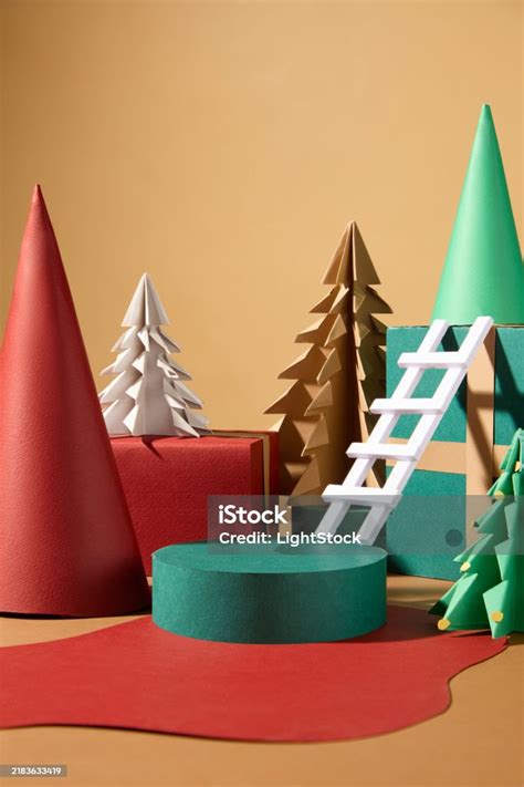 에메랄드 그린 포디움 중앙에 제품 전시 공간이 있고 그 옆에는 원뿔 모양의 포디움 크리스마스 선물 상자 사다리 베이지색 배경의 종이 소나무가 있습니다 크리스마스 테마 이미지