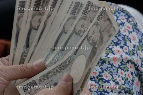 お札の束を膝の上で広げている女性の手元 たくさんのお金を手に持っているの写真素材 [255023653] イメージマート