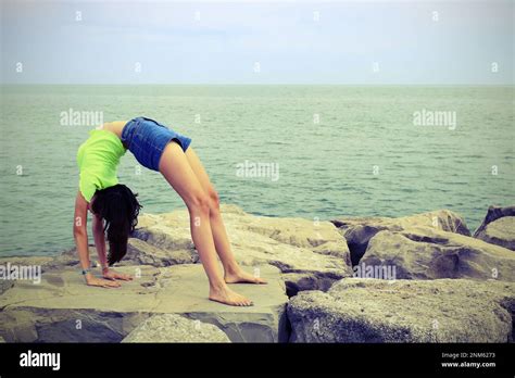 Young Girl Performs Gymnastic Exercises On The Rocks By The Sea With