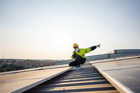 전문 엔지니어가 태양광 패널 시스템의 유지 보수를 위해 일합니다 지붕에서 일하는 매력적인 기술자는 일몰 동안 태양 전지 분야에서 태양 전지 패널 장비 상자를 검사하고