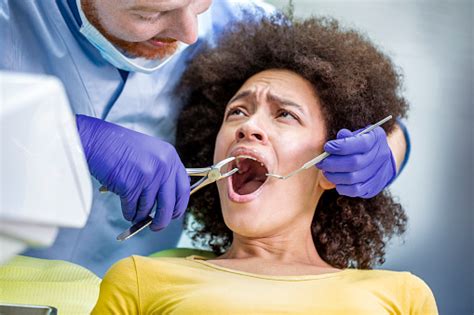 Dentist Using A Forceps To Pull A Tooth Out Of A Scared Patient Stock
