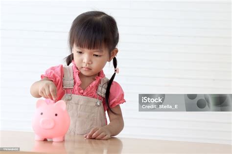 책상에 분홍색 돼지 저금통을 가진 행복한 미소 짓는 작은 아시아 소녀 아이 아이는 돼지 저금통에서 동전을 모으고 돈을 모으고 저축 또는 미래 개념을 위한 투자를 해야 합니다