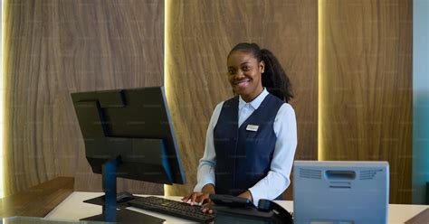 제복을 입은 행복한 젊은 성공적인 여성 접수원이 컴퓨터 모니터 앞에 카운터 옆에 서서 카메라를 보고 있다 사진 Unsplash의 미국 여자 이미지