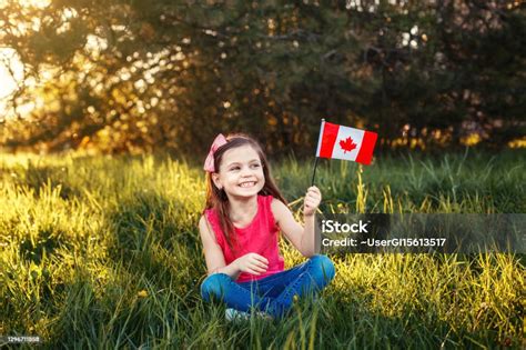 캐나다 국기를 들고 사랑스러운 귀여운 행복 백인 소녀 캐나다 국기를 들고 공원에서 잔디에 앉아 미소 아이 7 월 야외의 첫날에 캐나다의 날 휴가를 축하하는 어린이 시민