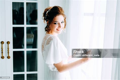 부드러운 우아한 젊은 갈색 머리 신부 창 대기 근처 다시 흰색 실내 서 입고 머리 머리 핀 신부 화장 신부의 여성의 내실입니다
