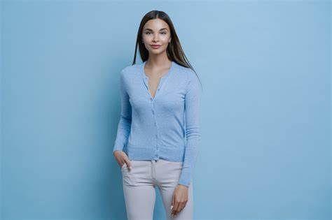 귀여운 열정적 인 여성은 슬림 한 그림을 가지고 캐주얼 점퍼와 흰색 청바지를 입고 주머니에 손을 유지 자신감 스탠드 친구와 함께