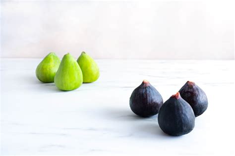 보라색 세 개와 녹색 무화과 세 개가 밝은 벽에 흰색 테이블에 놓여 있습니다 맛있는 잘 익은 향기로운 무화과는 수제 잼이나 보존을위한 훌륭한 성분입니다 가을 수확 건강한