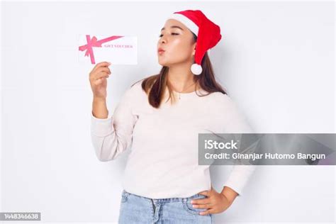 산타클로스 모자를 쓴 쾌활한 젊은 아시아 여성 20대가 흰색 스튜디오 배경에 격리된 손에 상품권 쿠폰 카드를 들고 키스합니다 메리 크리스마스 컨셉 25 29세에 대한 스톡