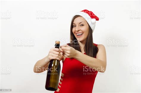 아름 다운 재미 있는 백인 젊은 행복 한 여자 빨간 드레스와 흰색 바탕에 샴페인 병을 열고 하려고 하는 크리스마스 모자에 매력적인 미소로 산타 소녀 격리입니다 새 해 휴일