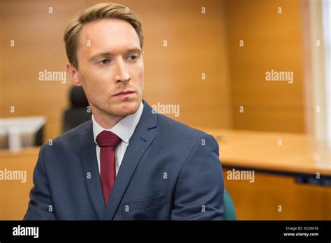 Man In His Thirties Sitting Behind Wooden Desk In Courtroom Wearing