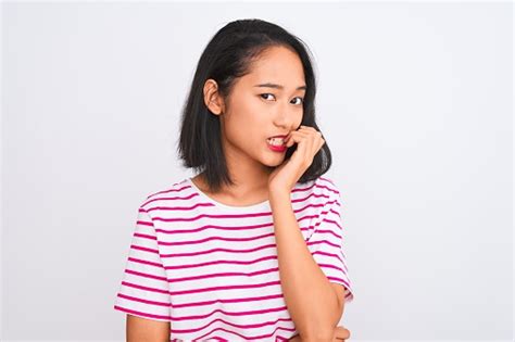 줄무늬 티셔츠를 입은 젊은 중국 여성은 손톱을 물고 손톱을 물고 손에 스트레스와 긴장 찾고 고립 된 흰색 배경 위에 서있다 불안 문제 T 셔츠에 대한 스톡 사진 및 기타