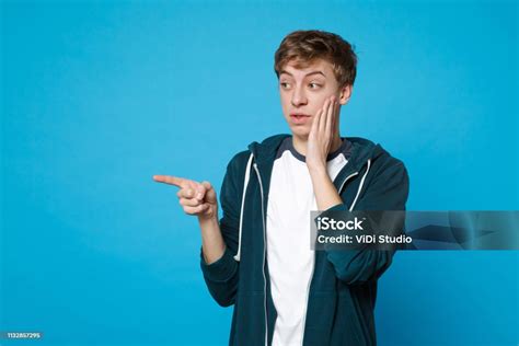 캐주얼에 당황 하는 혐오 젊은 남자는 뺨에 손을 퍼 팅 및 옆에 파란 벽 배경에 고립 된 검지 손가락 사람들은 진심으로 감정